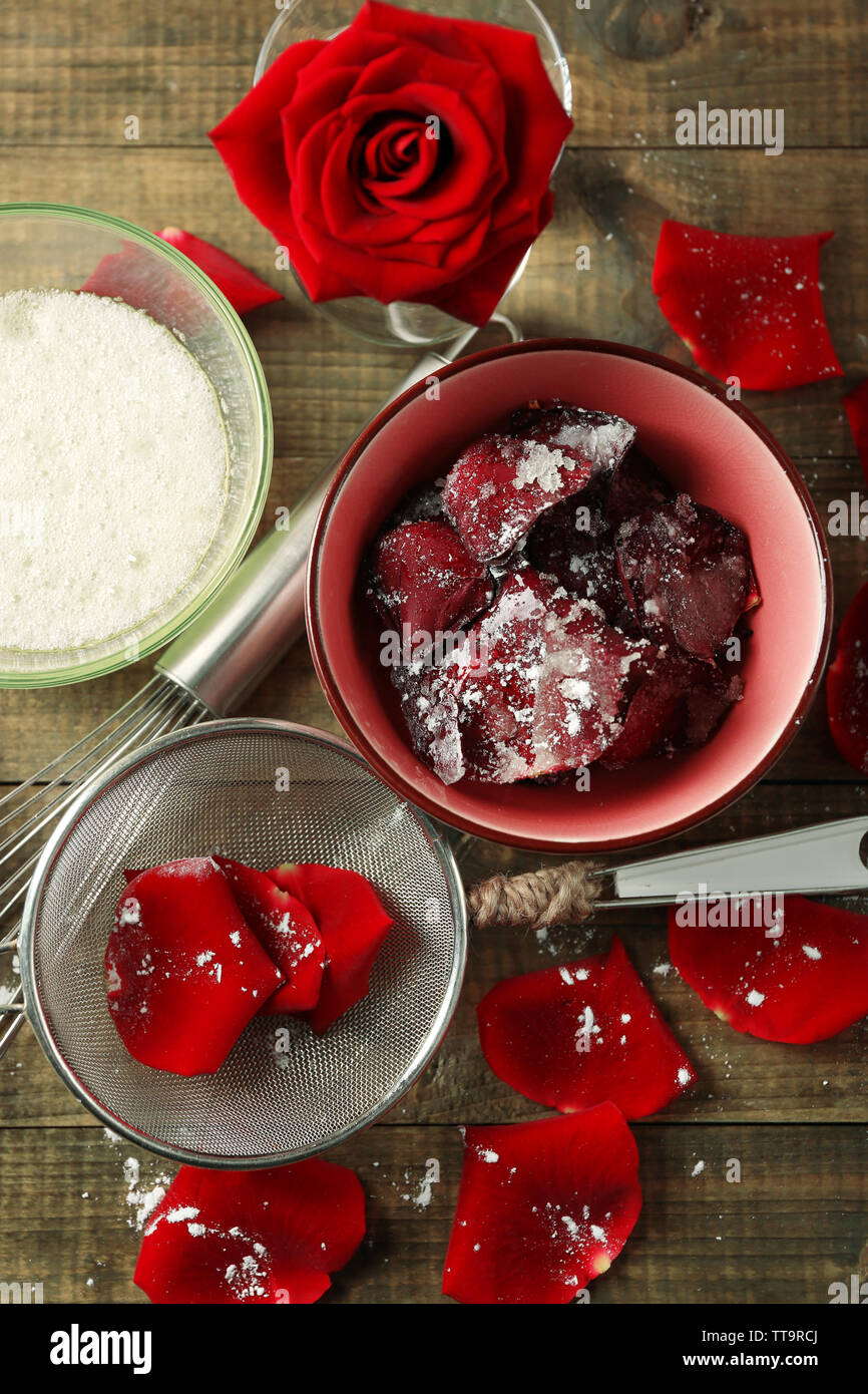 Making candied rose flower petals with egg whites and sugar, on wooden ...