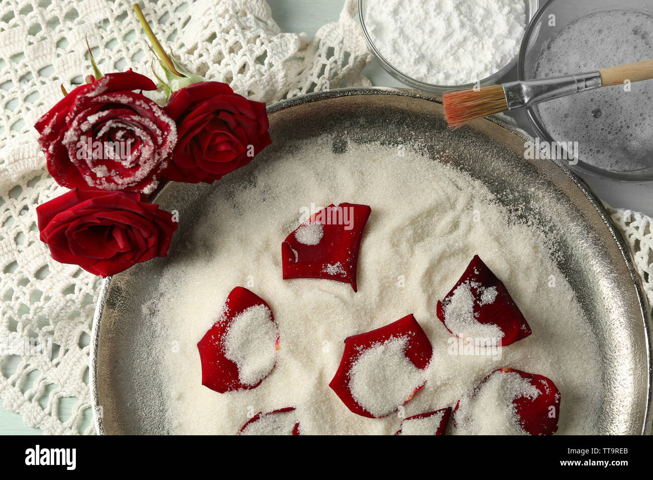 Making candied rose flower petals with egg whites and sugar, on wooden ...