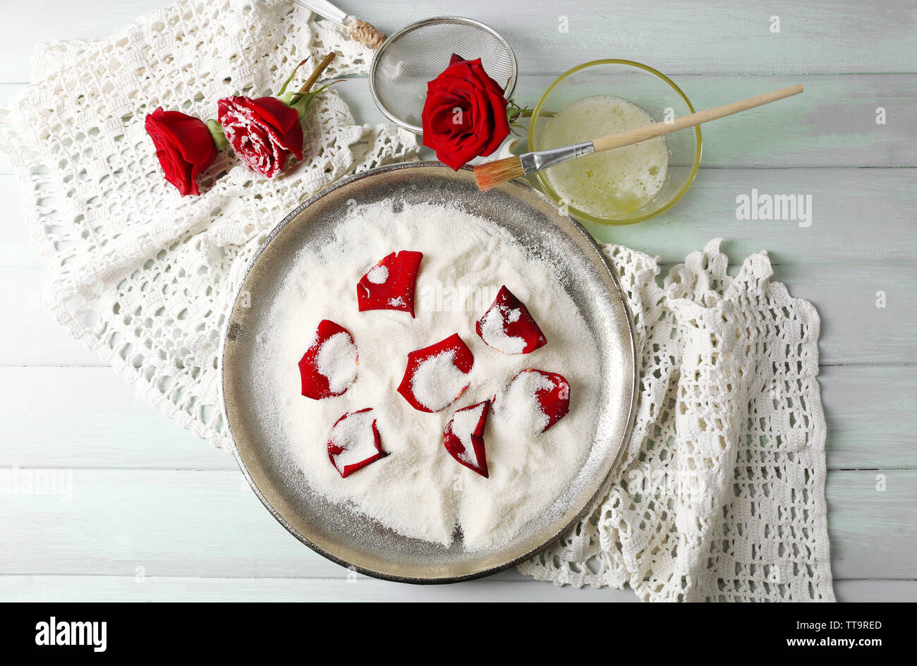 Making candied rose flower petals with egg whites and sugar, on wooden ...