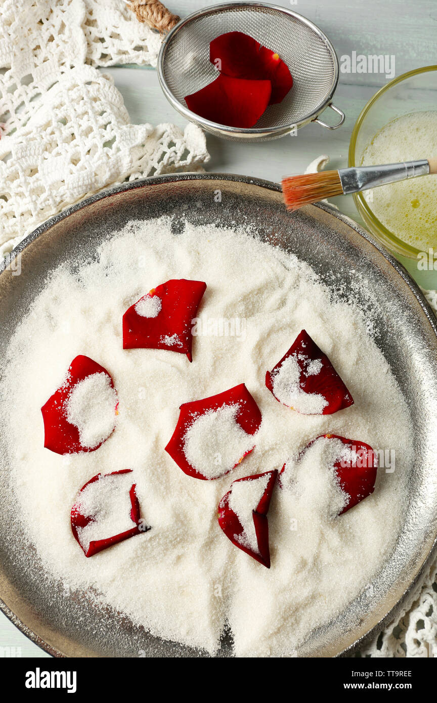 Making candied rose flower petals with egg whites and sugar, on wooden ...