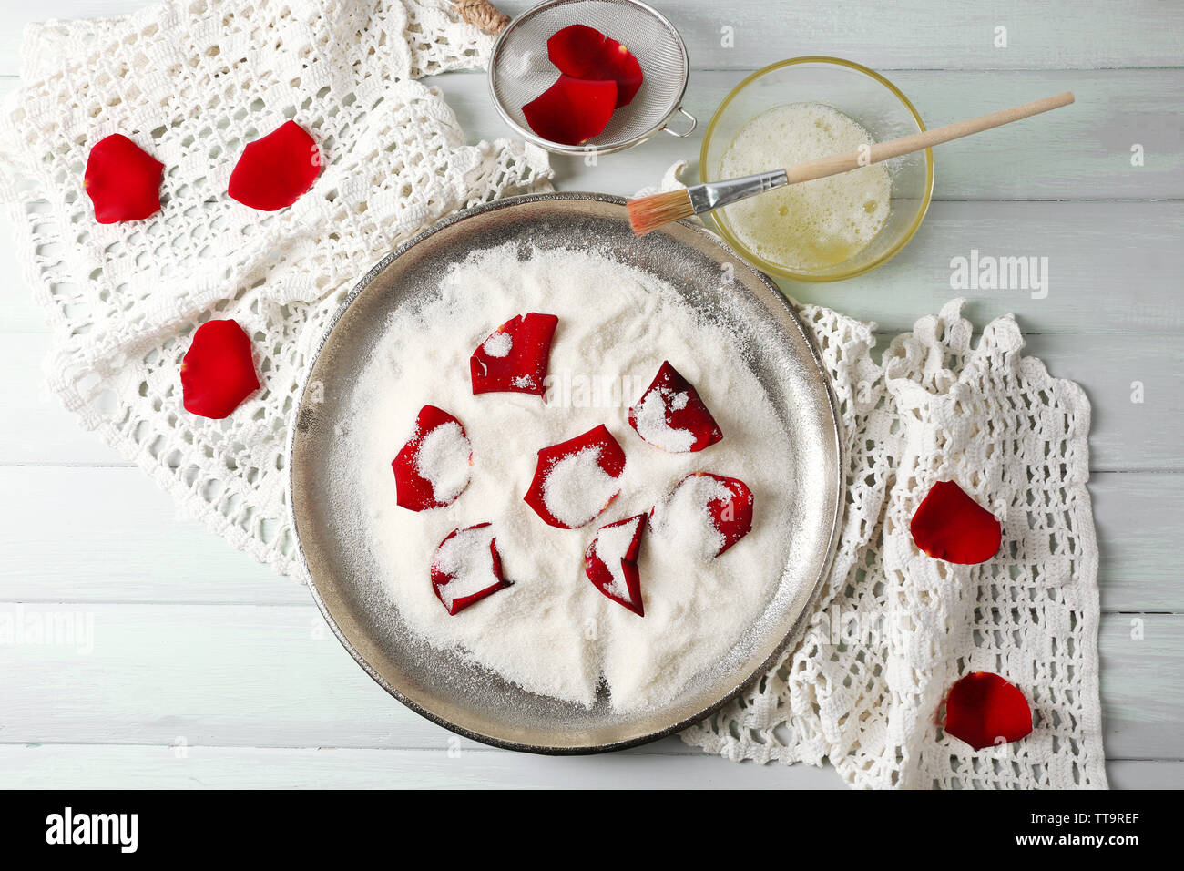 Making candied rose flower petals with egg whites and sugar, on wooden ...