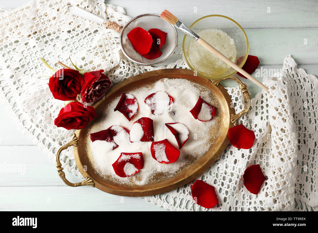Making candied rose flower petals with egg whites and sugar, on wooden ...