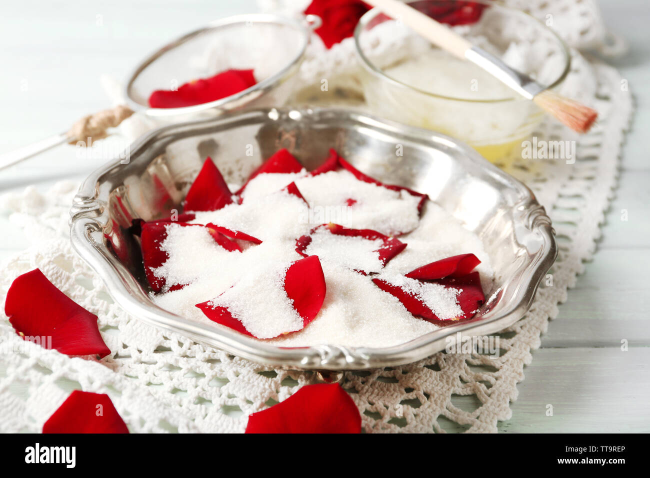 Making candied rose flower petals with egg whites and sugar, on wooden ...