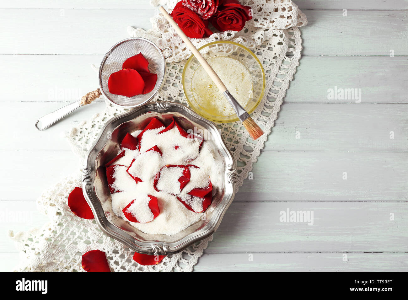 Making candied rose flower petals with egg whites and sugar, on wooden ...