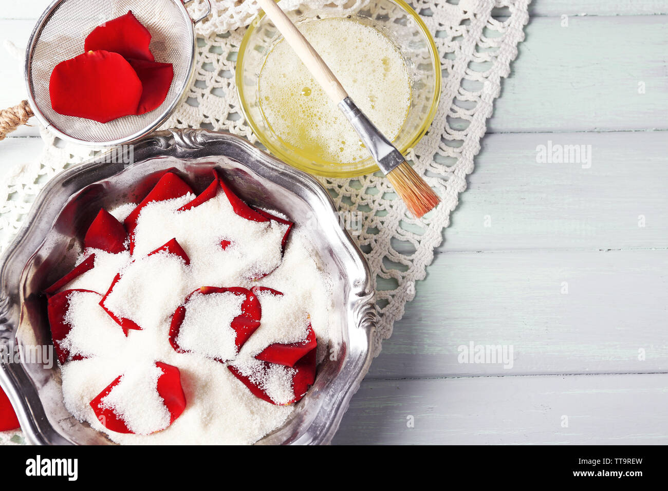 Making candied rose flower petals with egg whites and sugar, on wooden ...