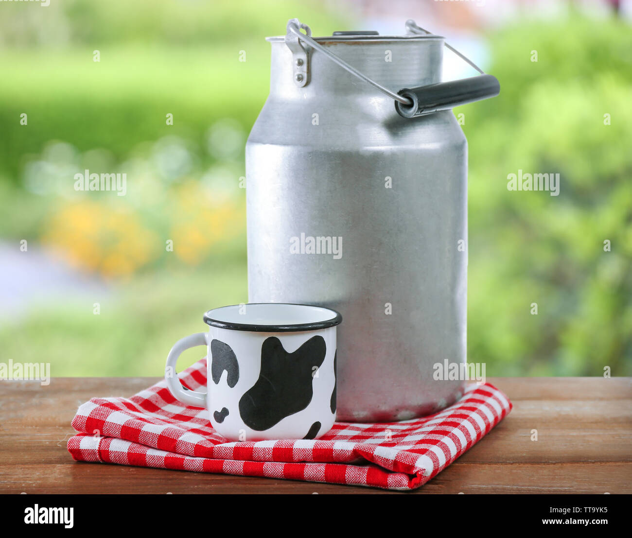 Retro can for milk and mug of milk on wooden table against blurred ...