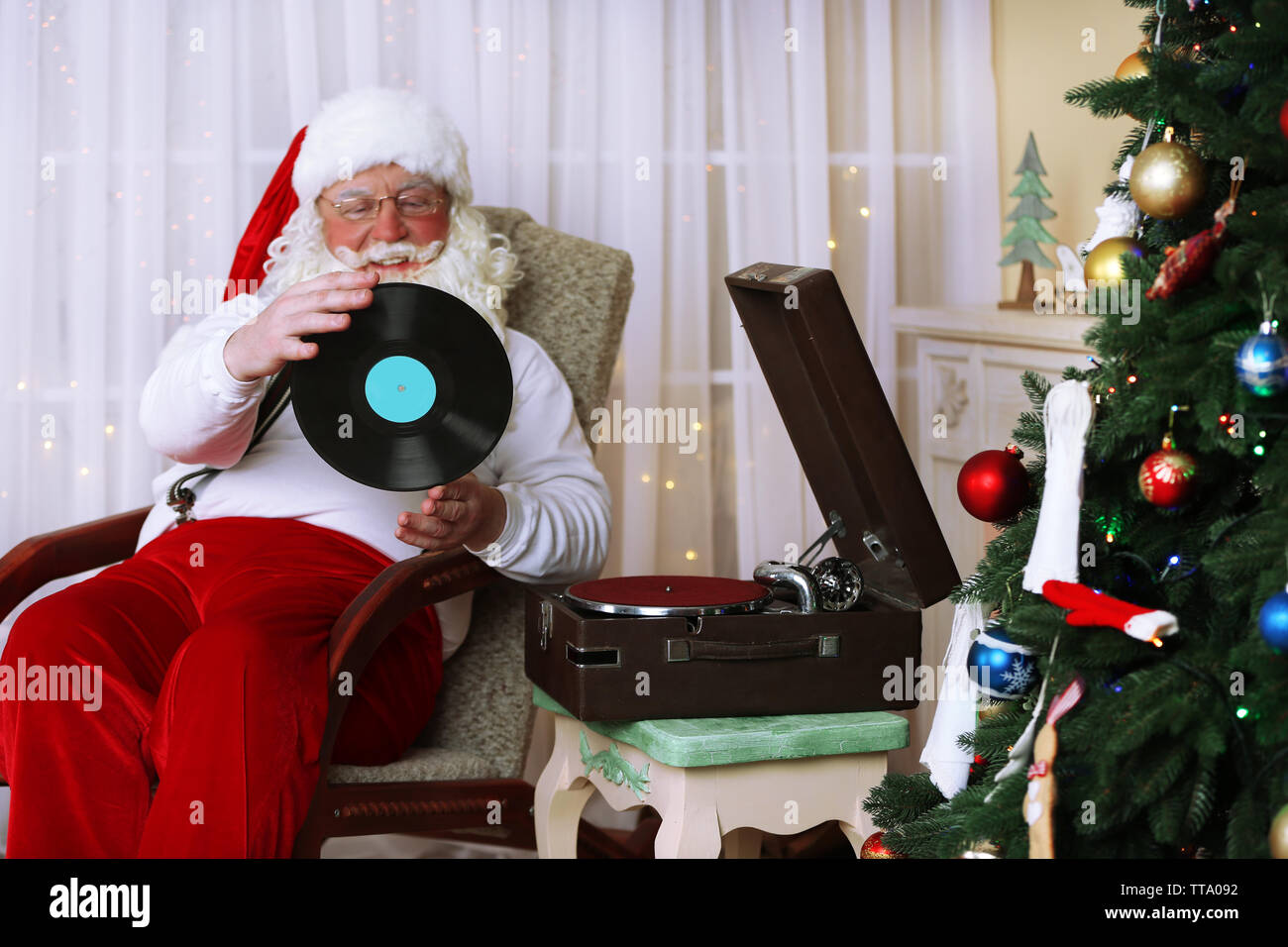 Santa Claus sitting in comfortable chair near retro turntable at home ...
