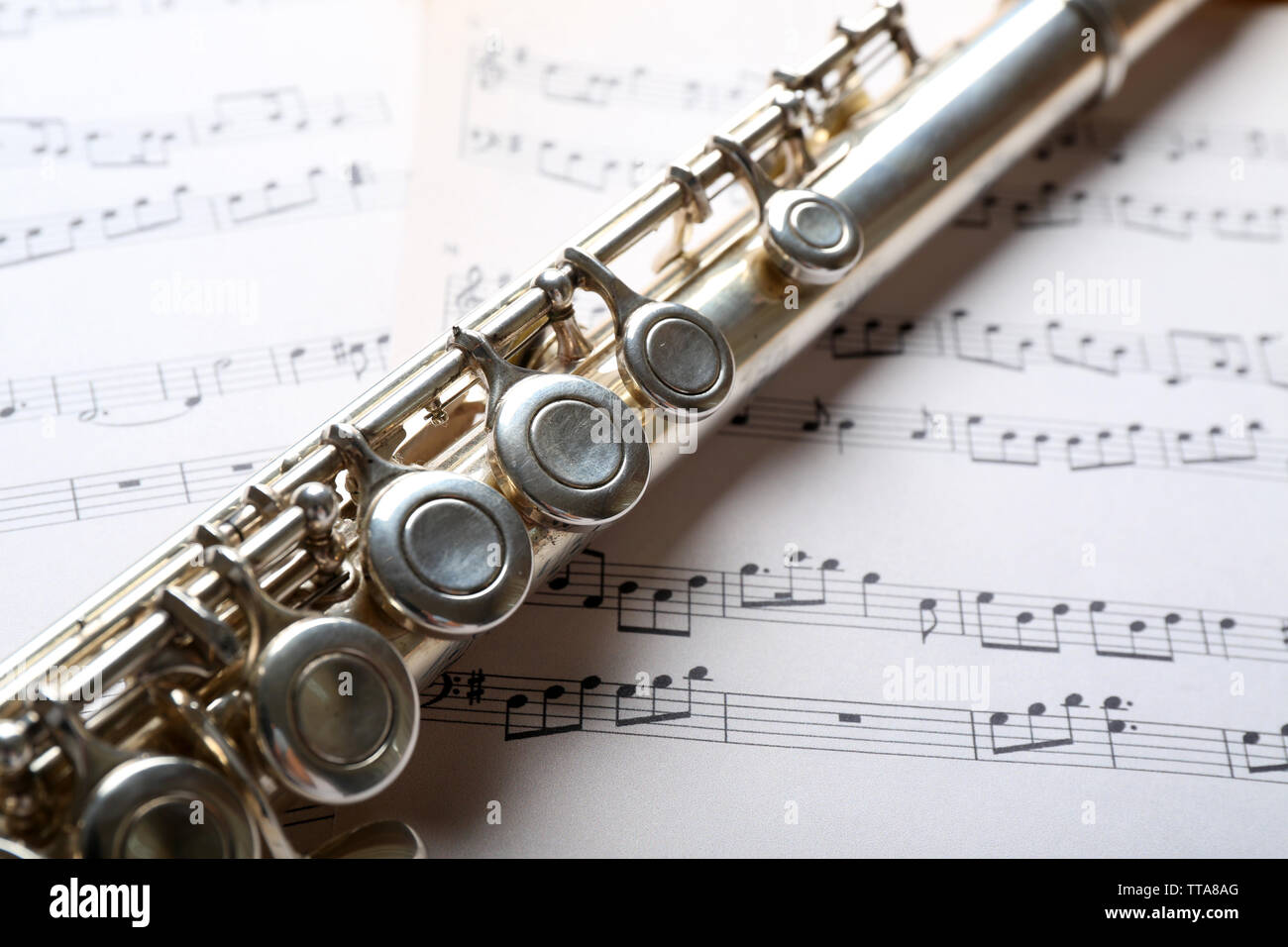 Silver flute on music notes background Stock Photo - Alamy