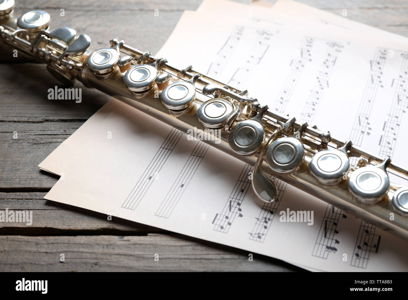 Silver flute with music notes on wooden table close up Stock Photo - Alamy