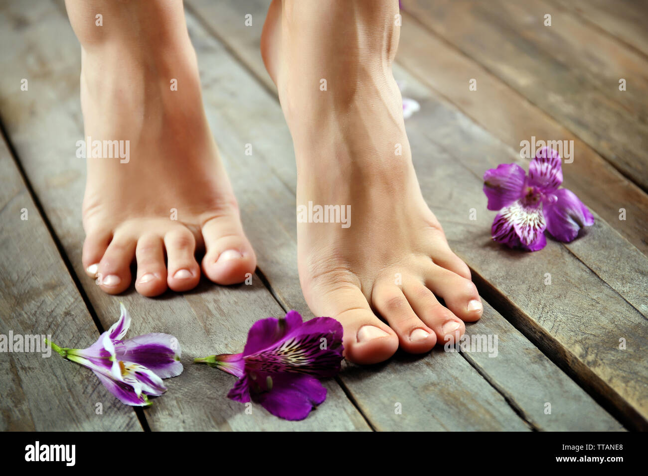 Female feet with flowers on wooden background Stock Photo - Alamy