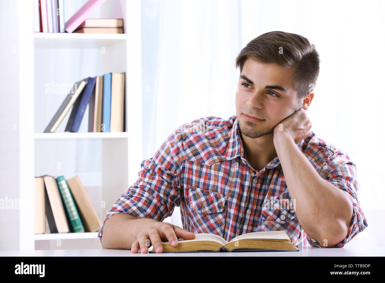 Young man reading book at table in room Stock Photo - Alamy
