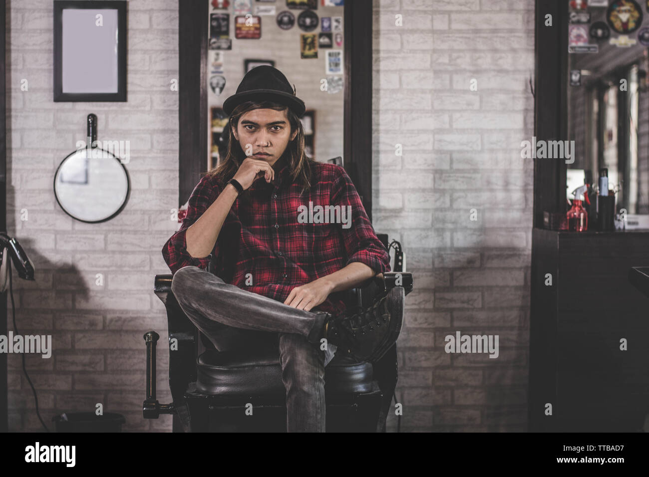 portrait of young man with long hair sitting at vintage barbershop ...