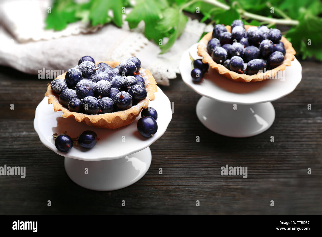 Delicious crispy tarts with black currants on white stand on wooden ...