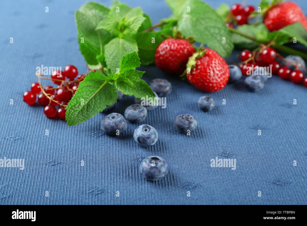 Group of fresh summer berries with mint on blue tablecloth background ...