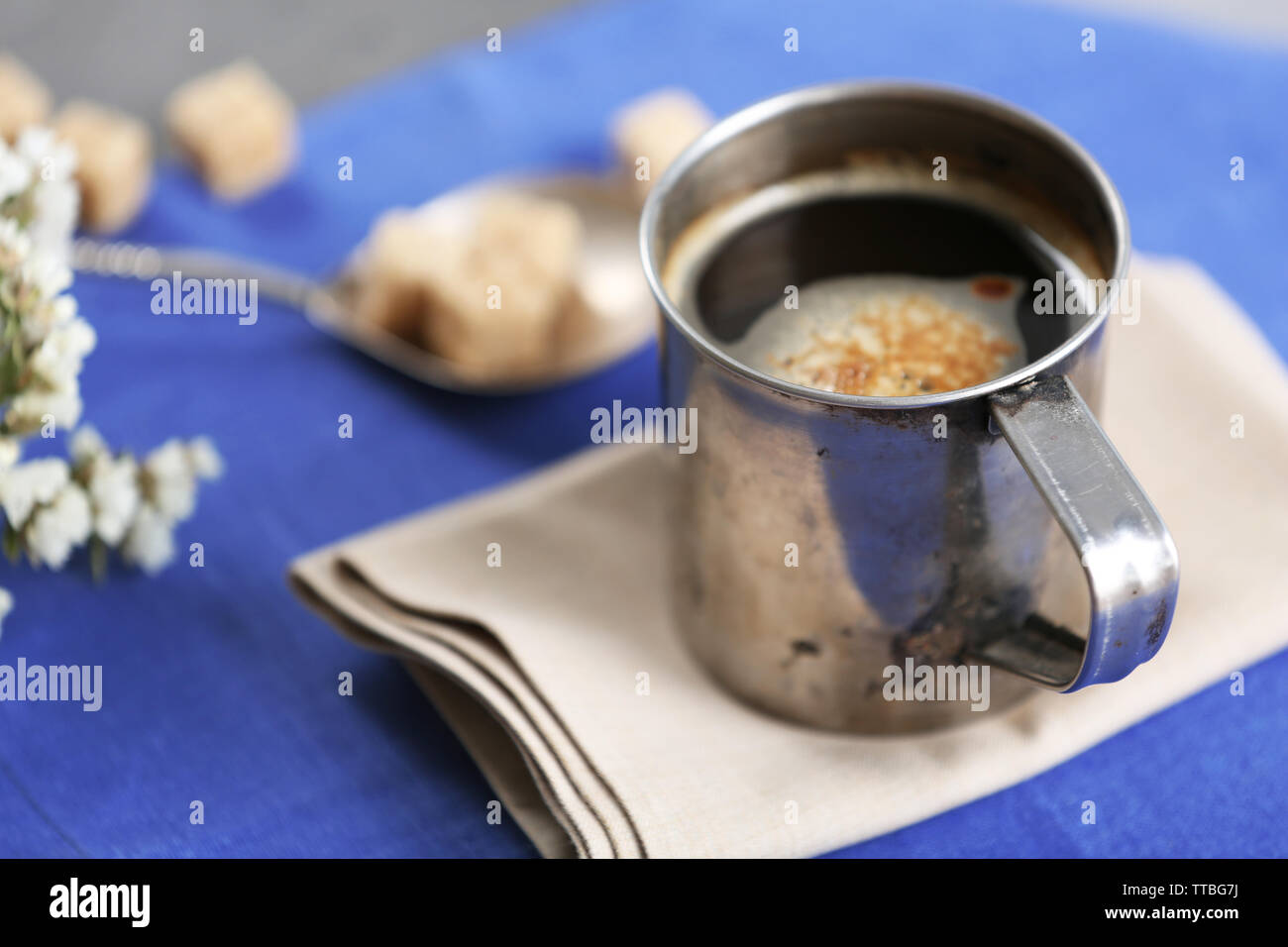 Metal cup of flavored coffee with lump sugar and flowers on table with ...