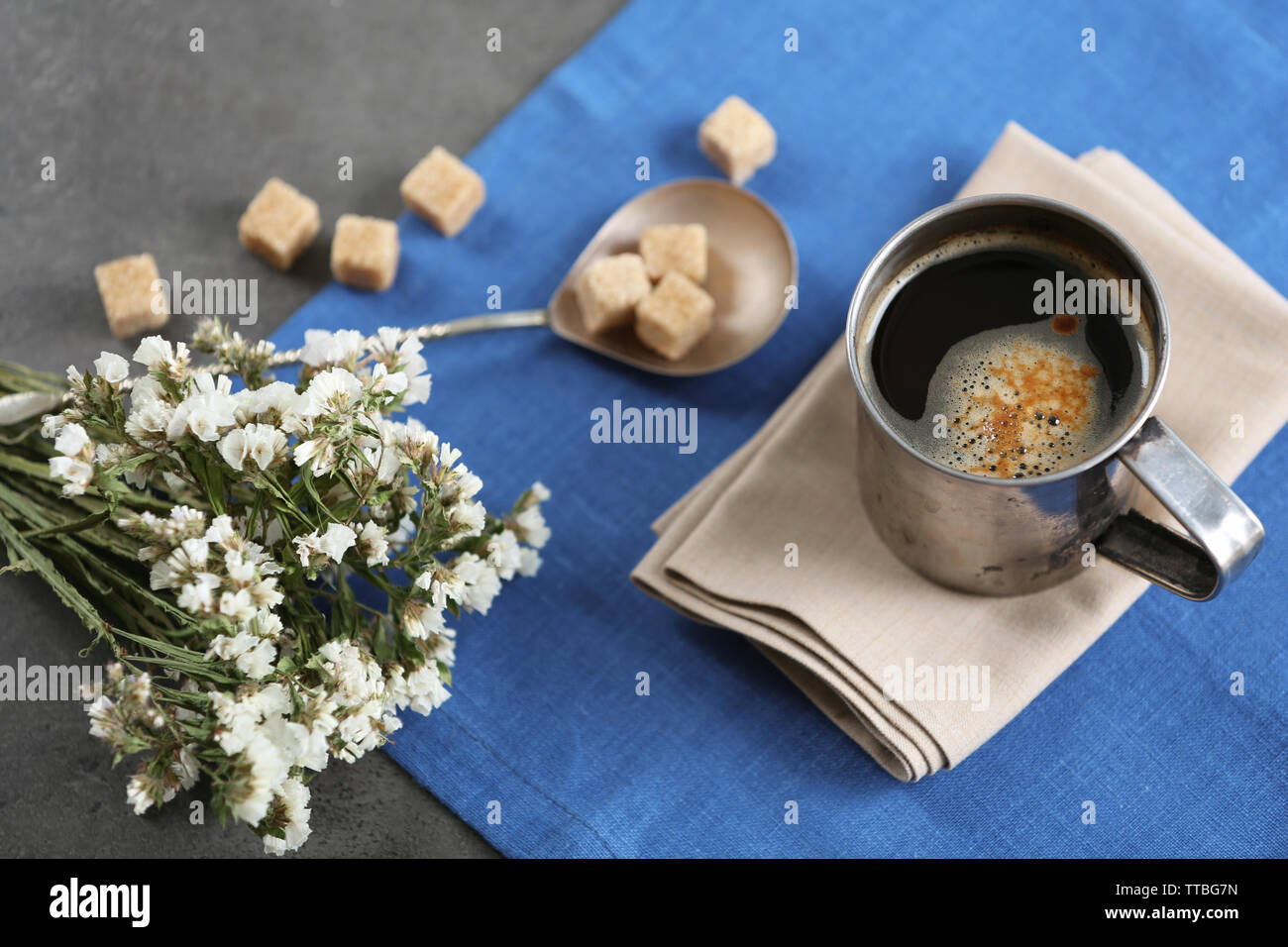 Metal cup of flavored coffee with lump sugar and flowers on table with ...
