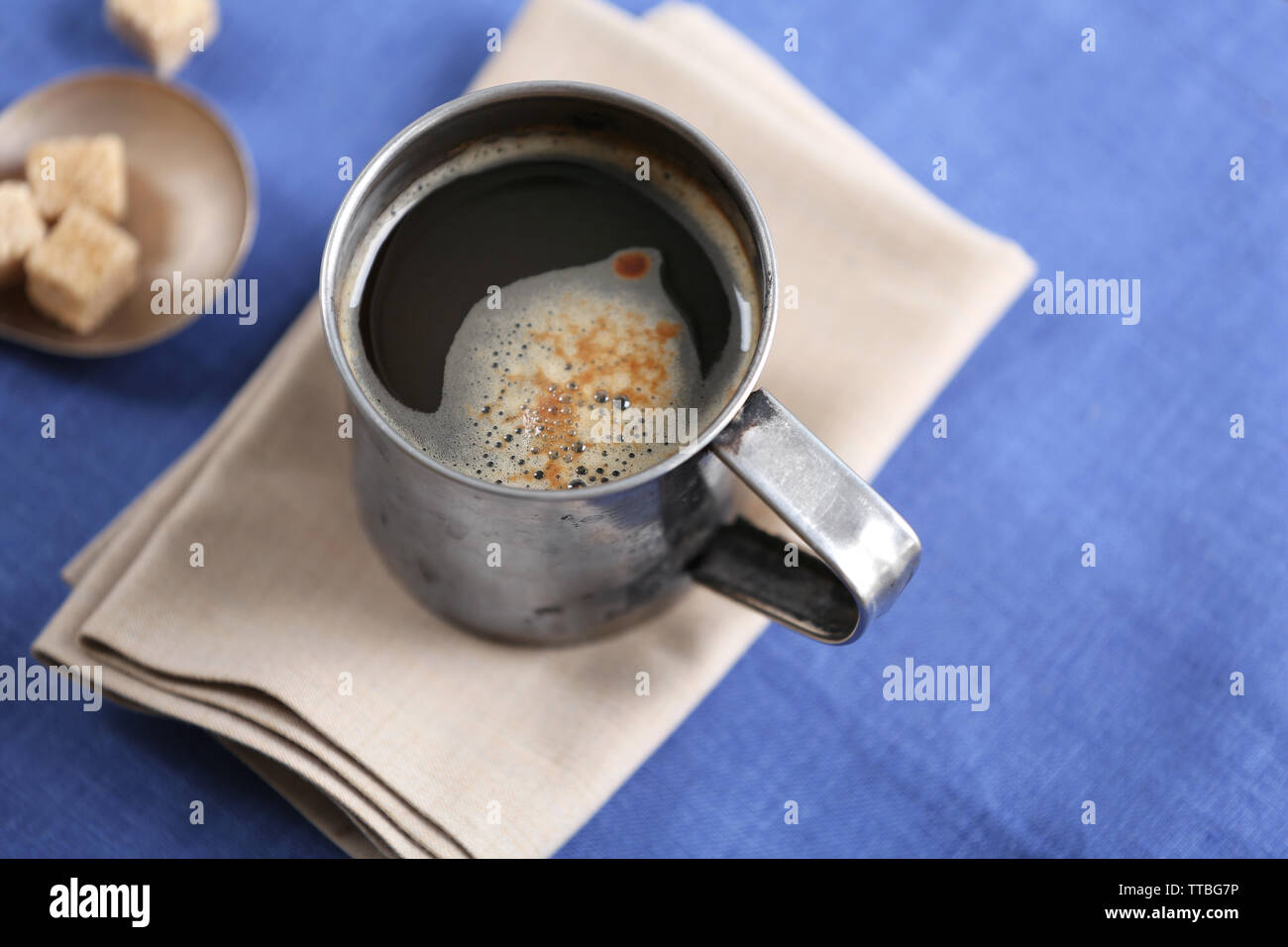 Metal cup of flavored coffee with lump sugar and flowers on table with ...