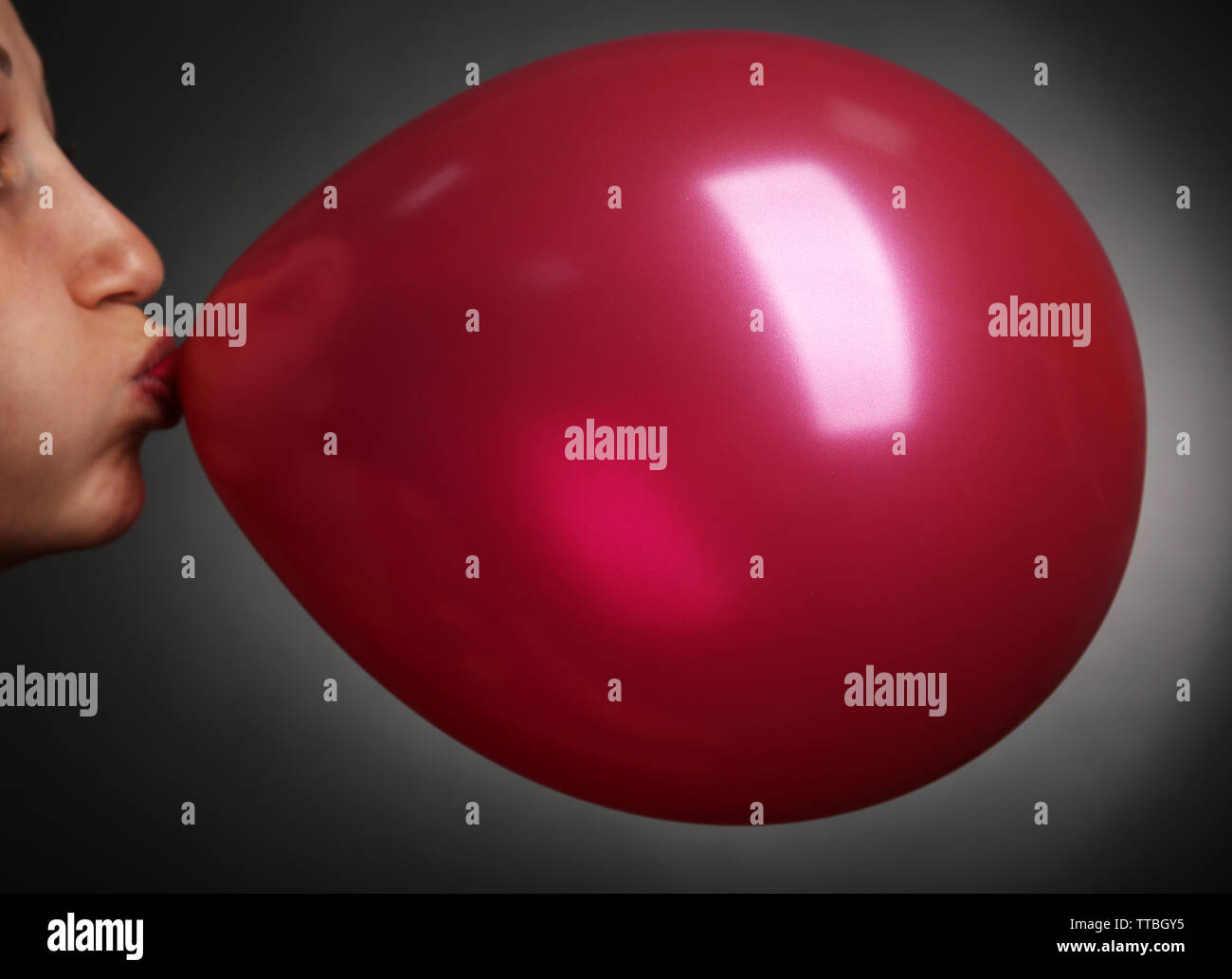 Young woman inflating balloon on gray background Stock Photo - Alamy