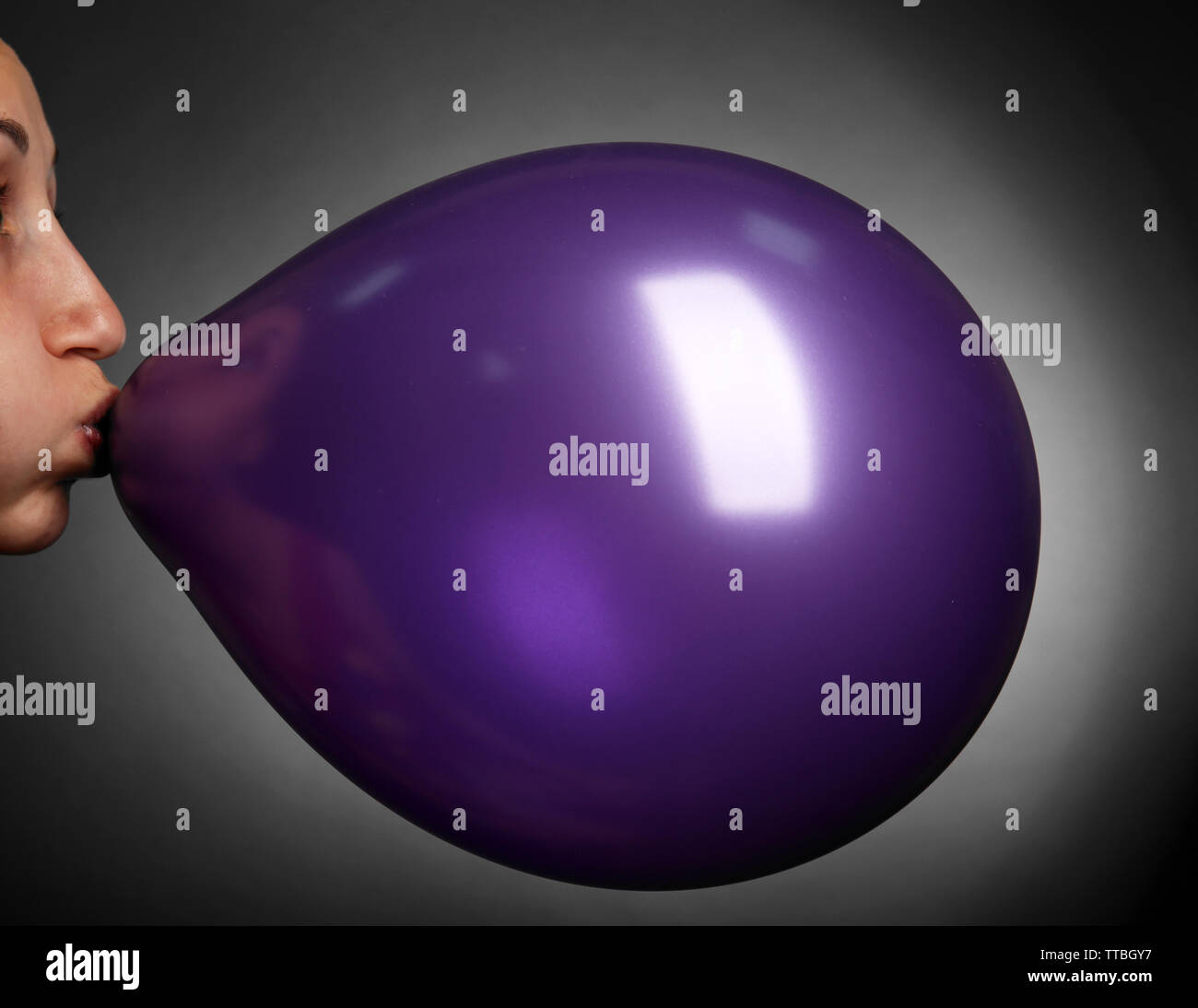 Young woman inflating balloon on gray background Stock Photo - Alamy