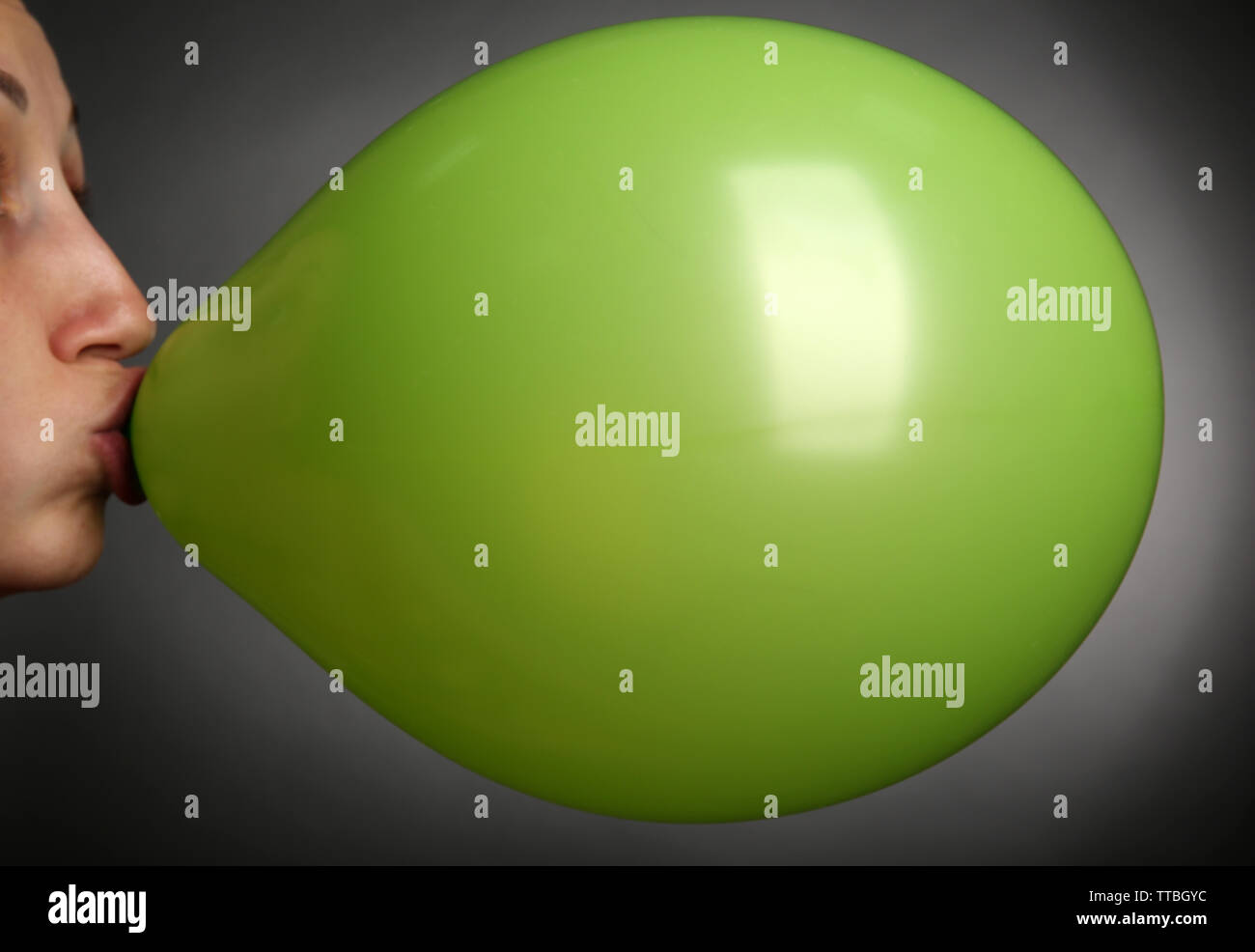 Young woman inflating balloon on gray background Stock Photo - Alamy