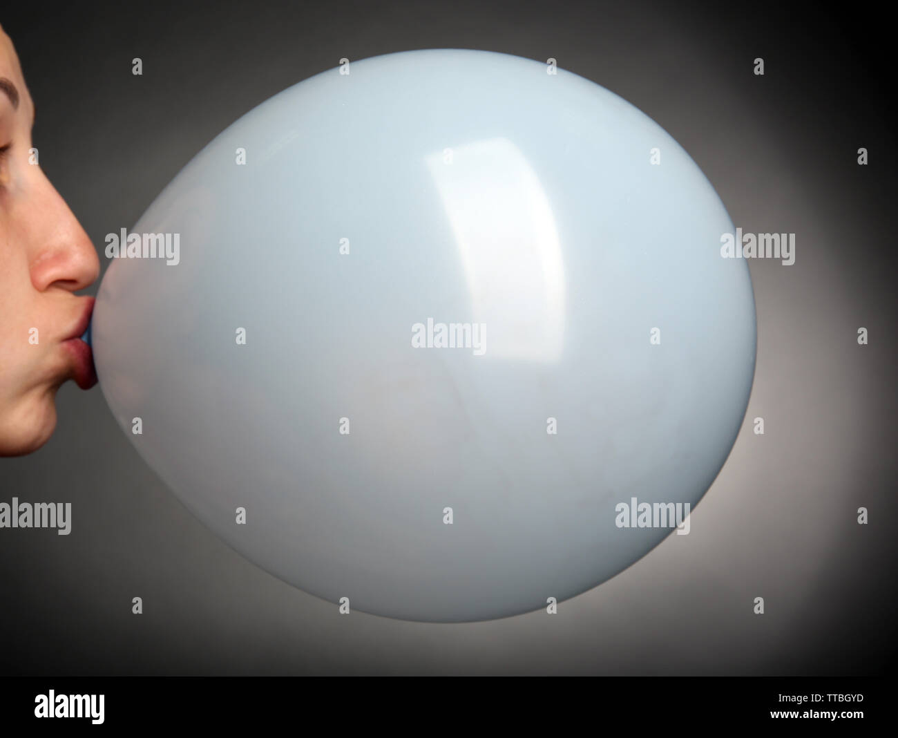 Young woman inflating balloon on gray background Stock Photo - Alamy