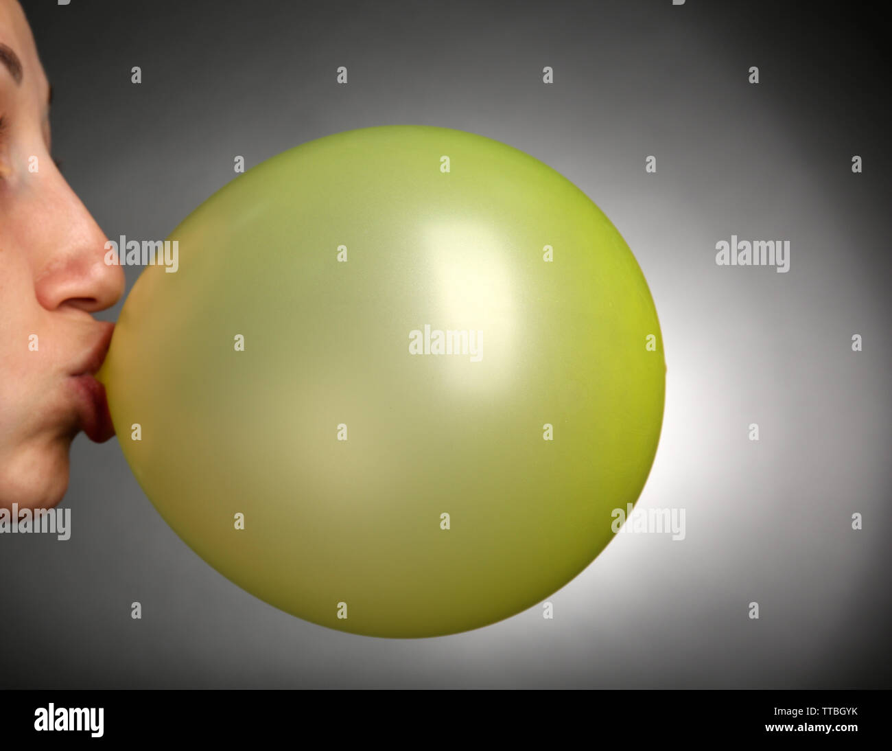 Young woman inflating balloon on gray background Stock Photo - Alamy