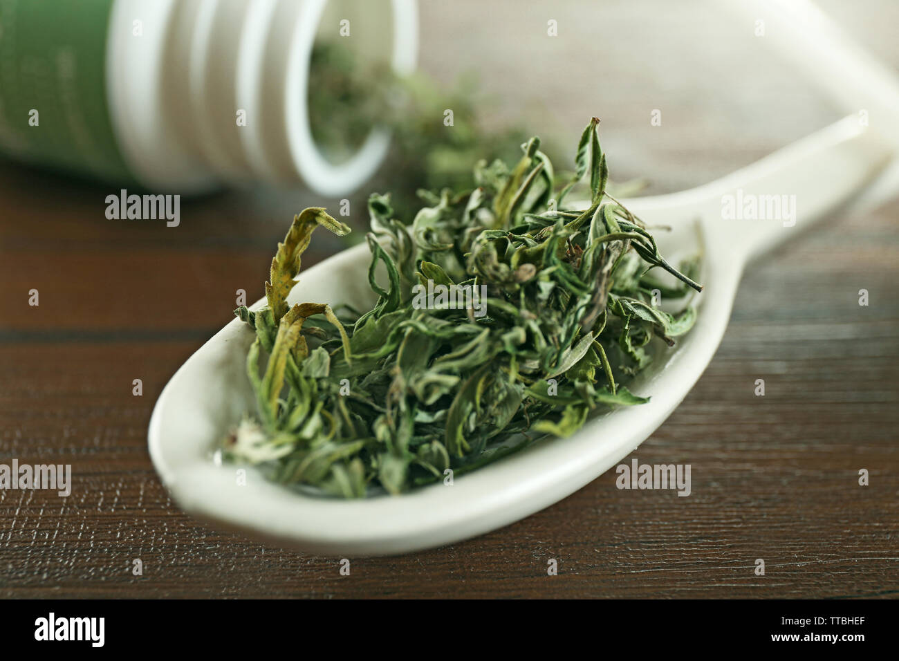 Bottle of medical cannabis with dry herbs in spoon on table close up ...