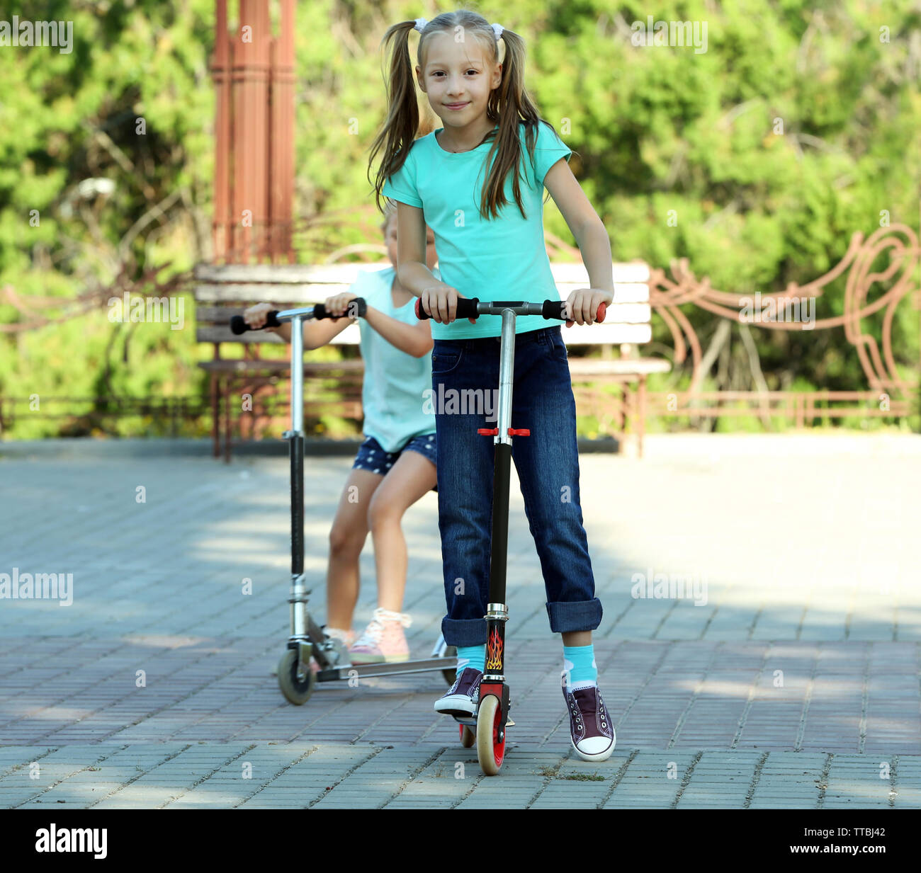 Small girls riding on scooters in park Stock Photo - Alamy