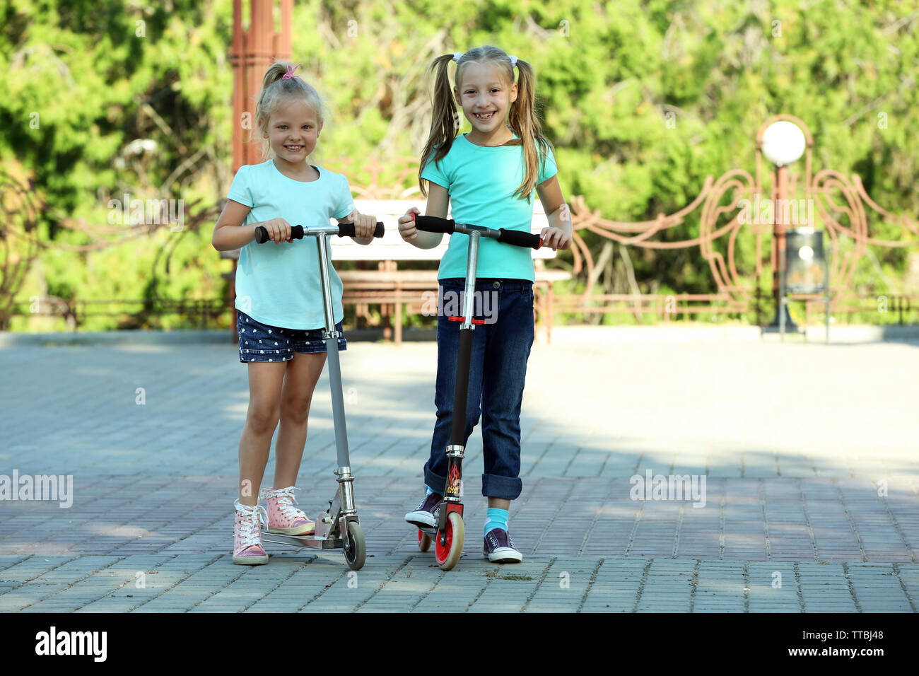 Small girls riding on scooters in park Stock Photo - Alamy