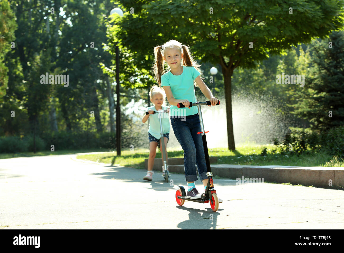 Small girls riding on scooters in park Stock Photo - Alamy
