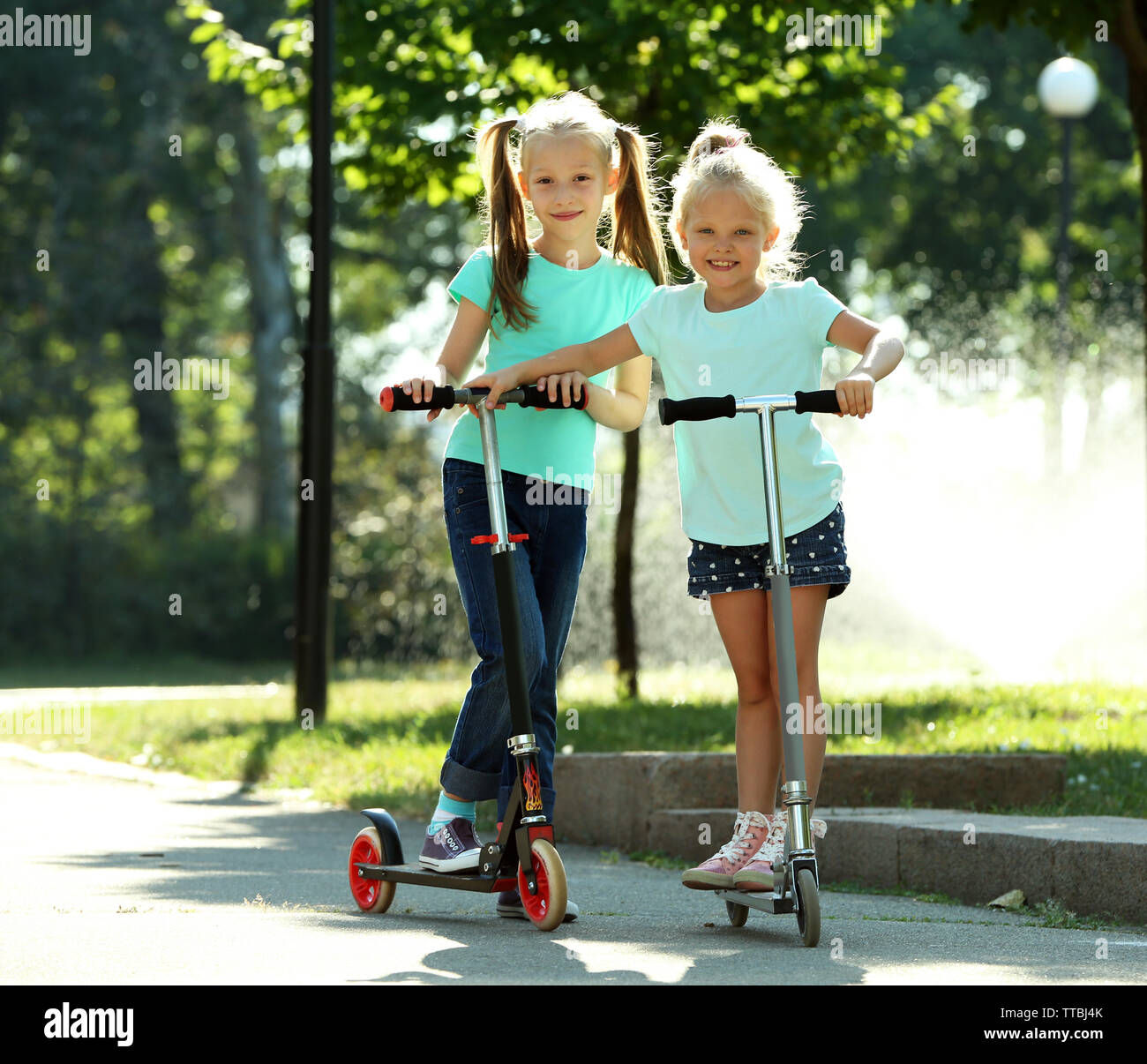 Small girls riding on scooters in park Stock Photo - Alamy