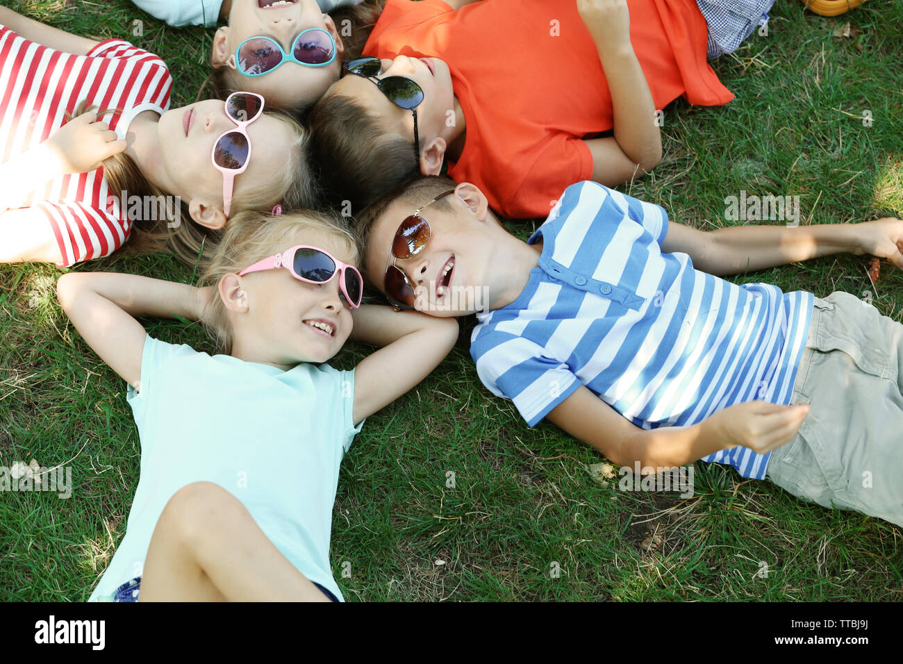 Happy active children lying on green grass in park Stock Photo - Alamy