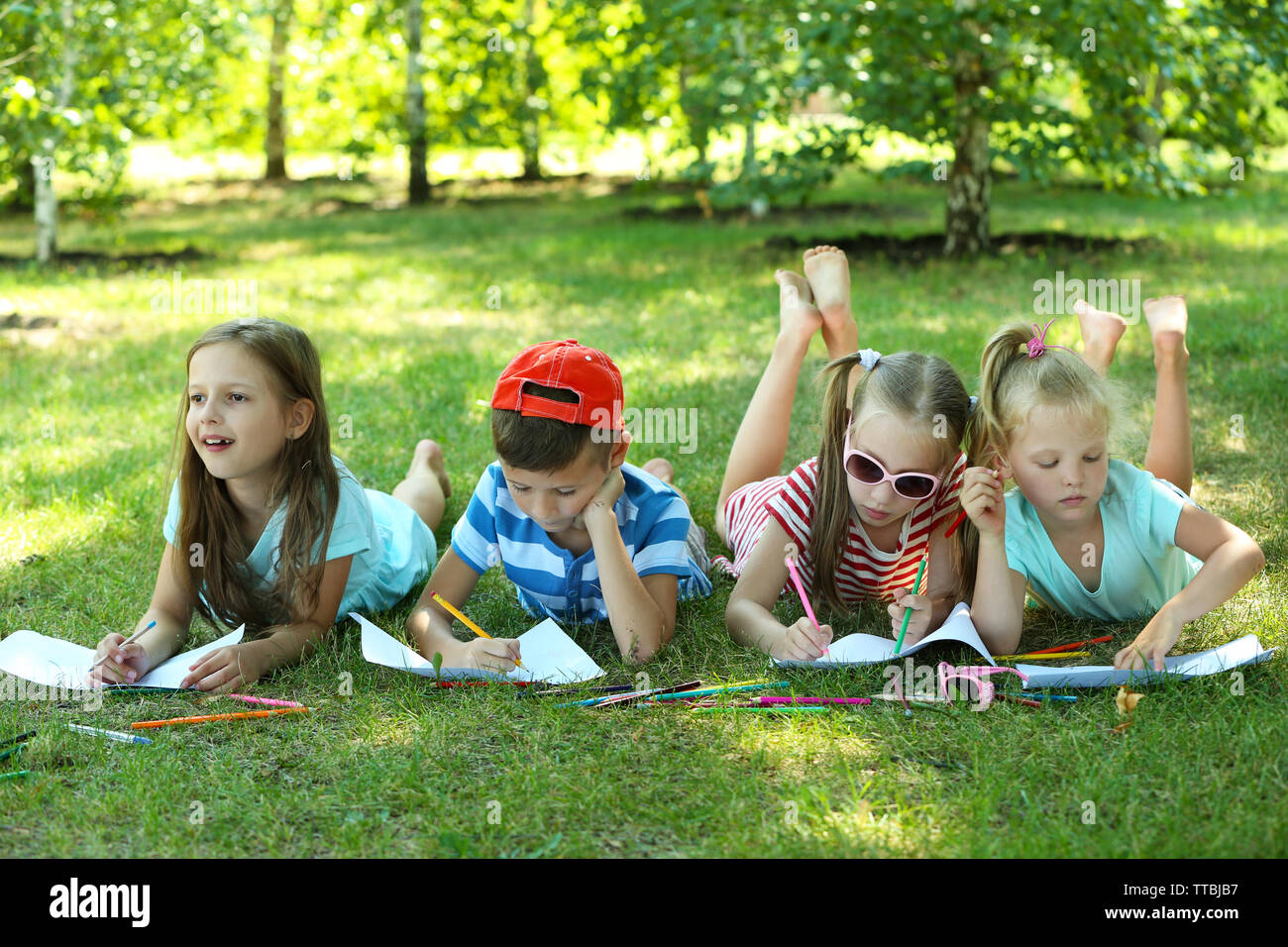 Happy active children lying on green grass and drawing in park Stock ...