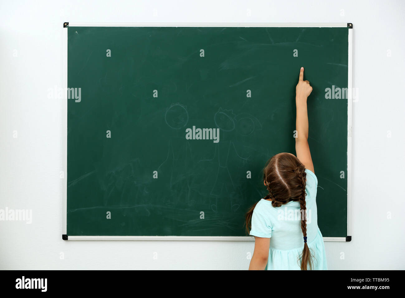 Little girl pointing at something at black chalkboard in classroom ...