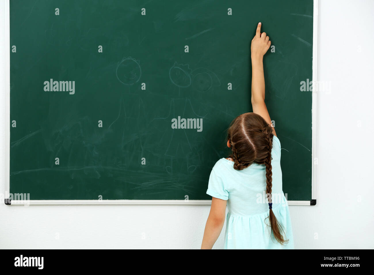 Little girl pointing at something at black chalkboard in classroom ...
