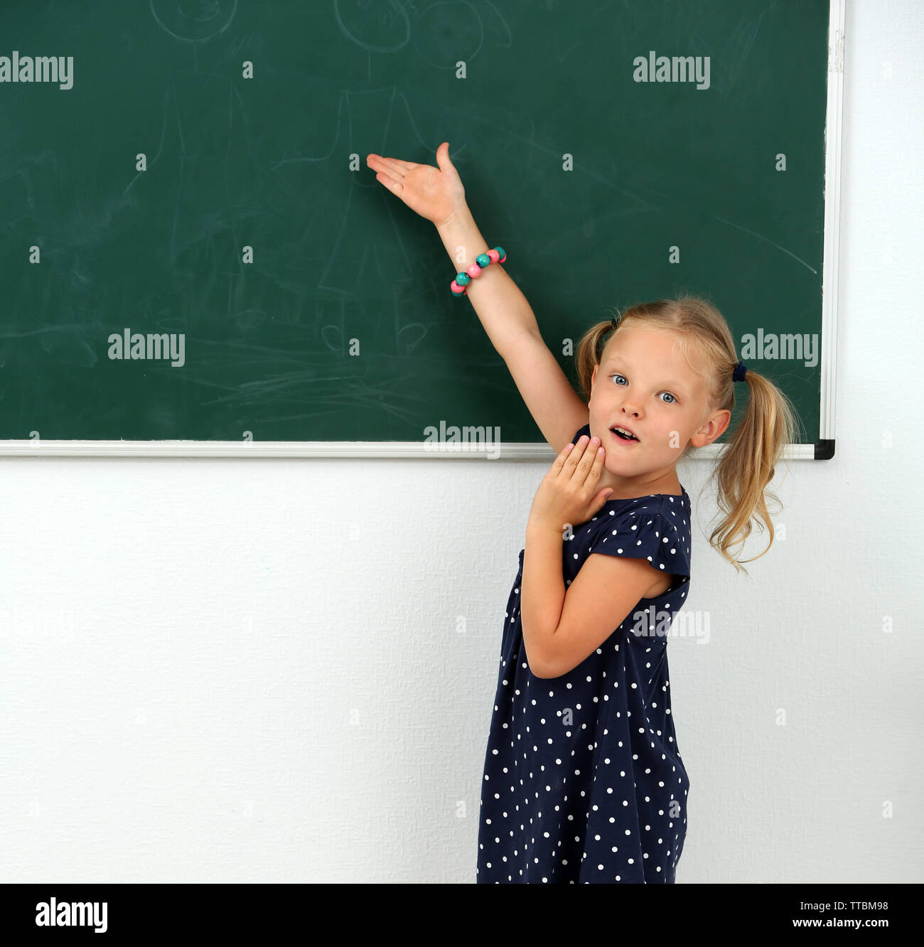 Little girl pointing at something at black chalkboard in classroom ...