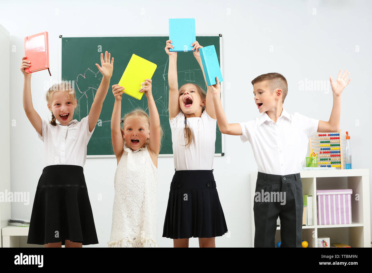 Portrait of happy classmates with books looking at camera in classroom ...