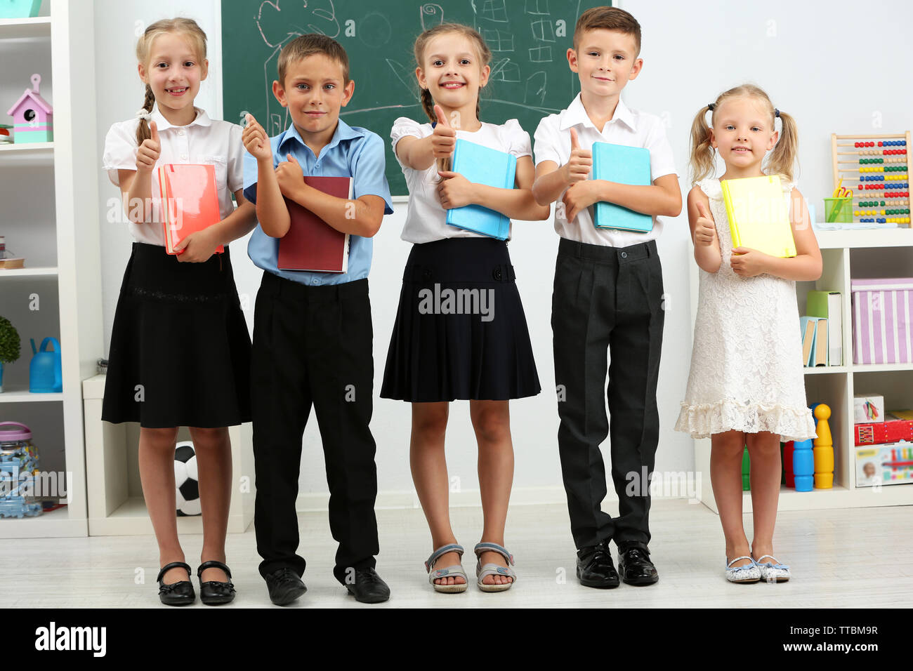 Portrait of happy classmates with books looking at camera in classroom ...