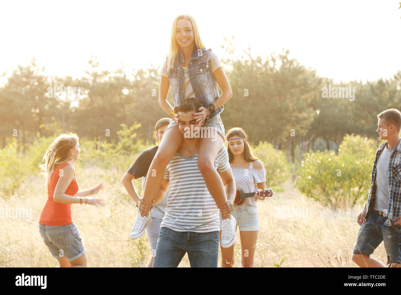 Joyful friends relaxing, a girl on guy's shoulders in the forest ...
