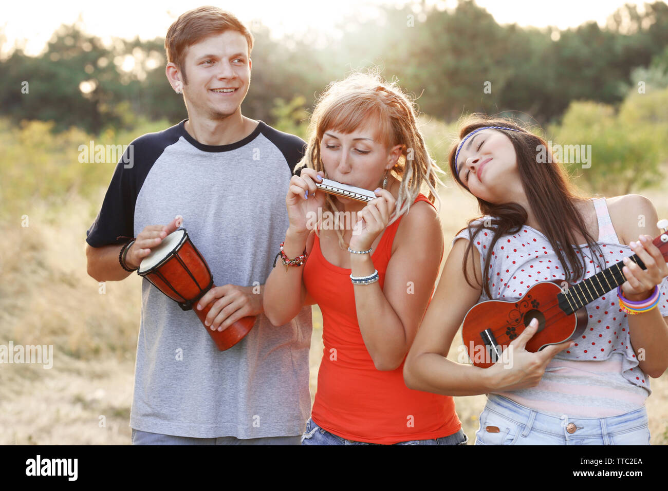 Happy smiling friends playing musical instruments in the forest ...