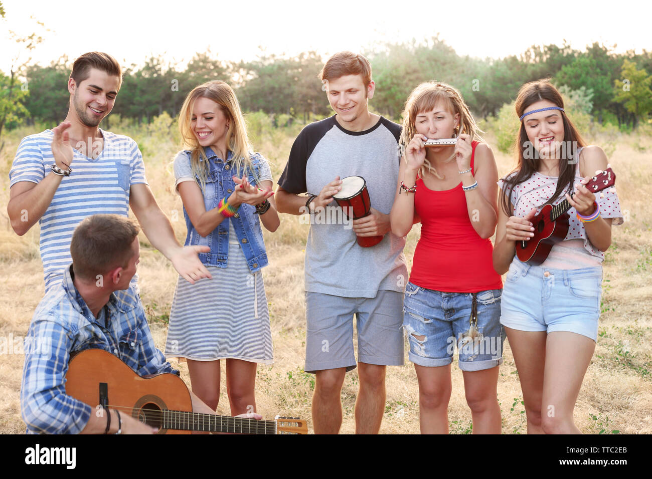 Happy smiling friends playing musical instruments in the forest ...