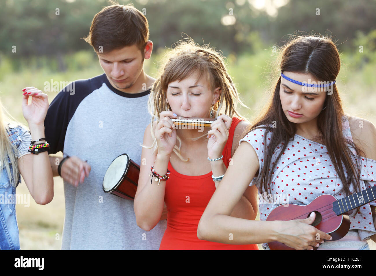 Happy smiling friends playing musical instruments in the forest ...