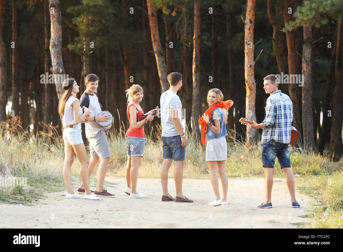 Happy smiling friends playing musical instruments in the forest ...