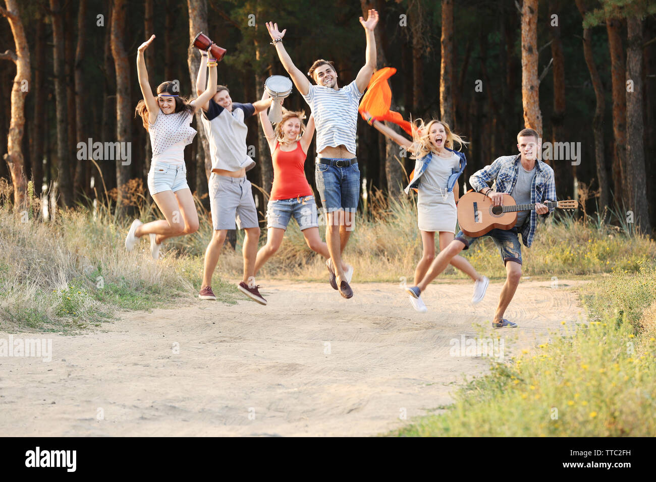 Happy smiling friends with musical instruments jumping in the forest ...