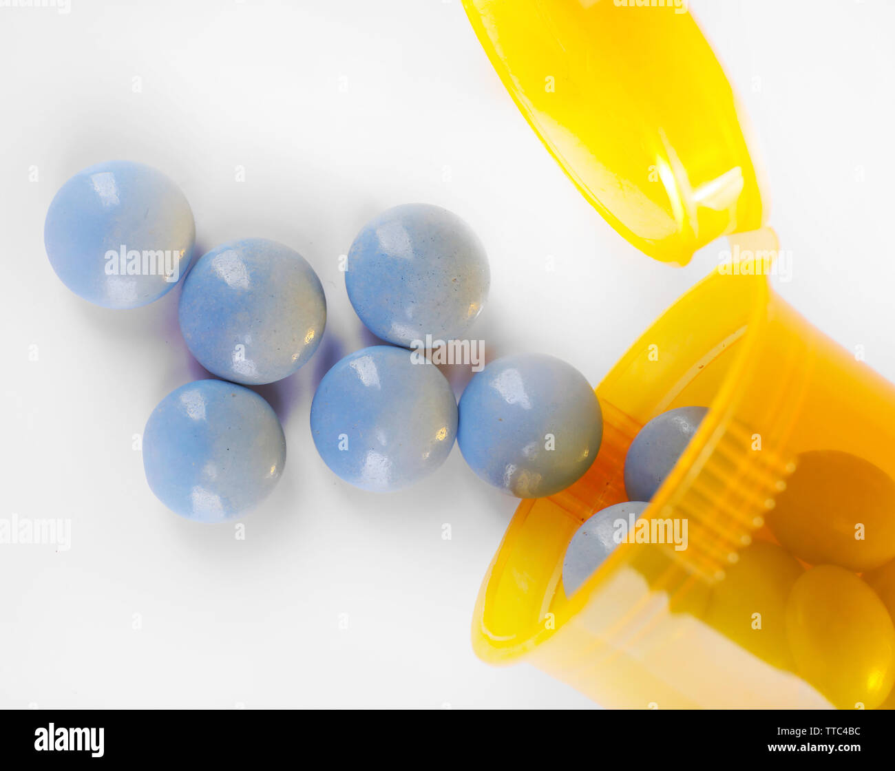 Blue drugs spilled from yellow pill bottle on white background, close ...