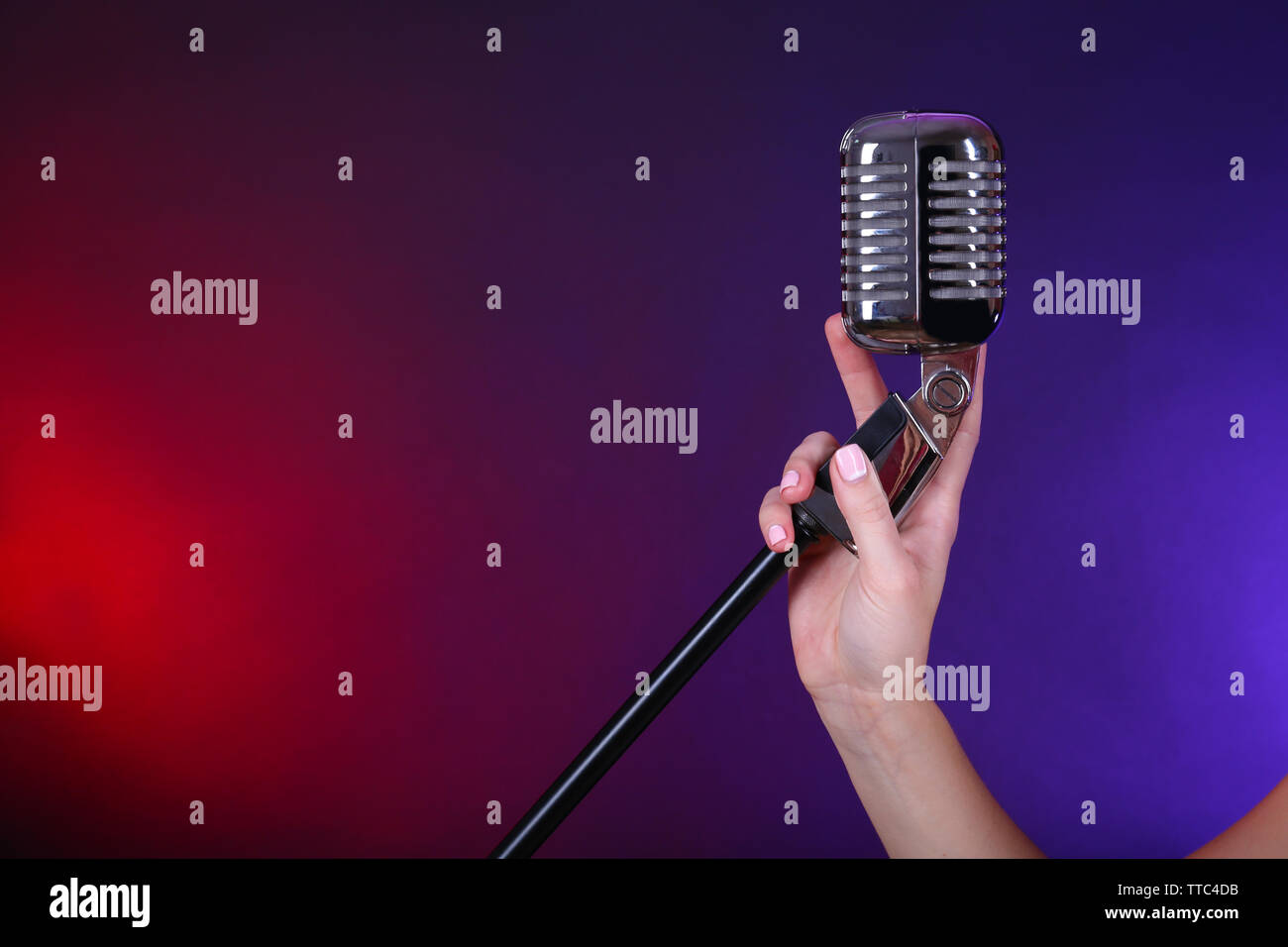 Female hand holding a retro microphone against colourful background ...