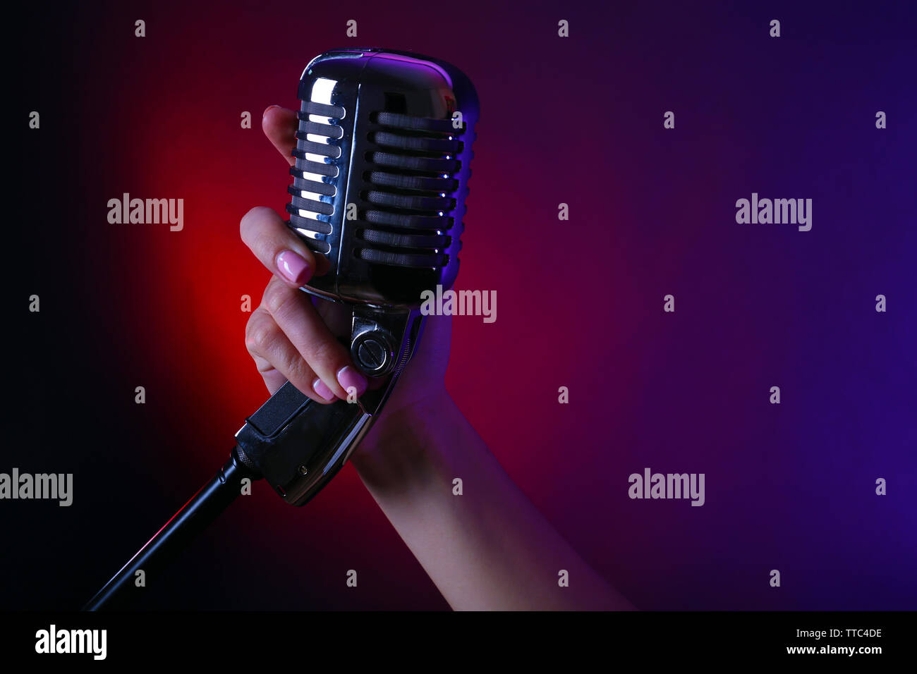 Female hand holding a retro microphone against colourful background ...