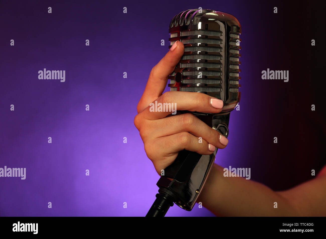 Female hand holding a retro microphone against colourful background ...