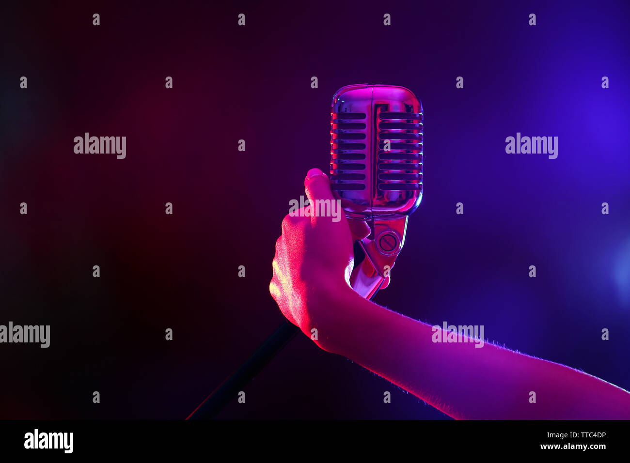 Female hand holding a retro microphone against colourful background ...