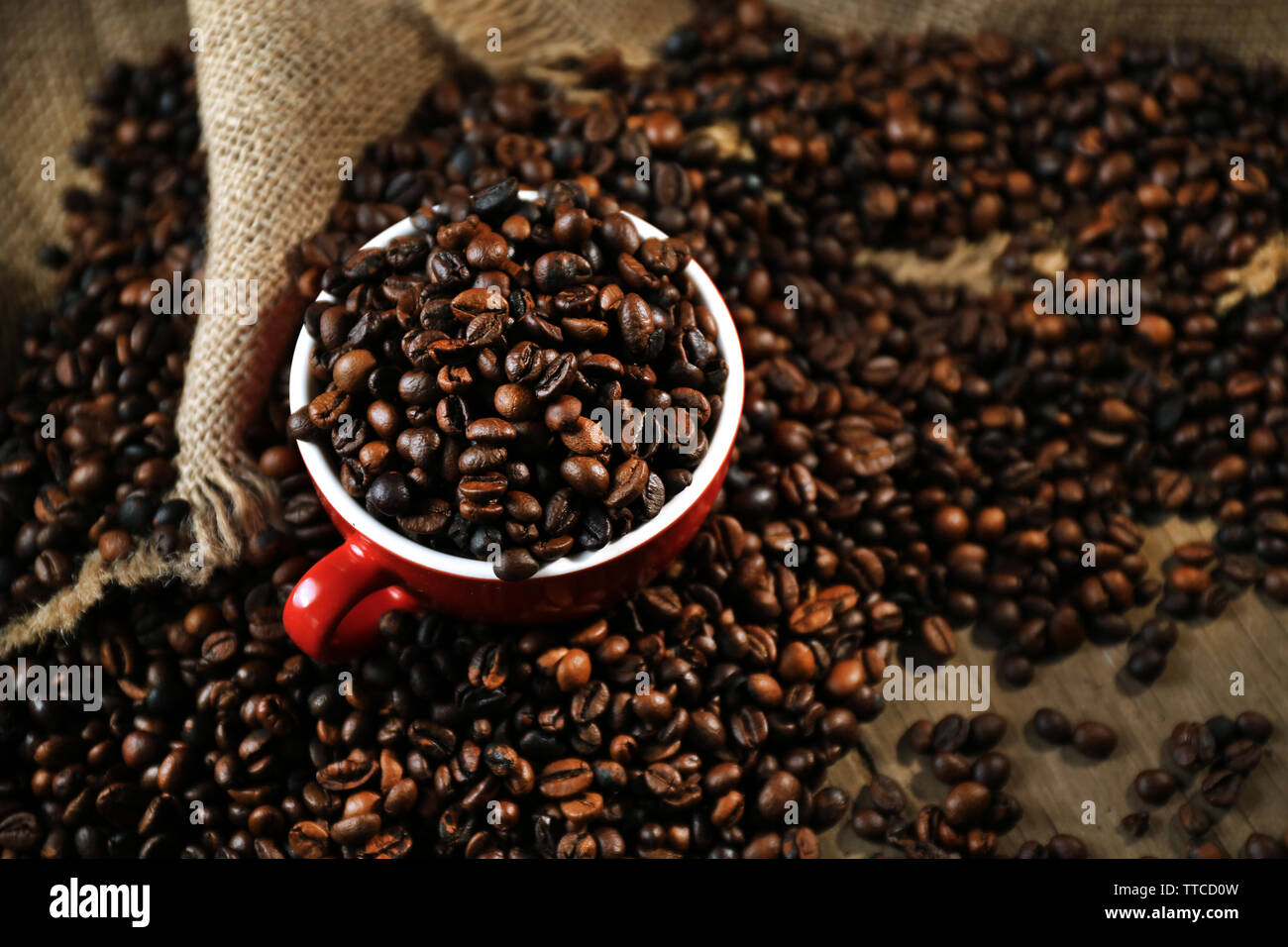 A red cup and aromatic coffee beans scattered on sacking background ...
